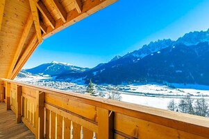 Varanda de madeira com vista para montanhas cobertas de neve e um vale.