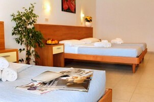 Quarto de hotel com cama, mesa de cabeceira, planta e luminária fixada na parede.