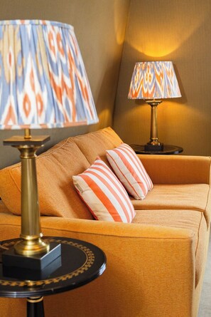 Quarto de hotel com sofá, duas almofadas listradas e duas luminárias com cúpulas estampadas.