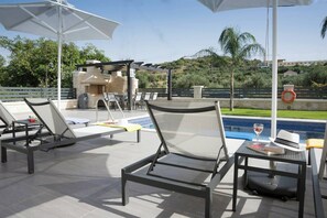 Área ao lado da piscina com espreguiçadeiras, guarda-sóis e piscina.