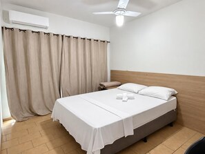 Cama bem arrumada com lençóis brancos, cabeceira de madeira e ventilador de teto.