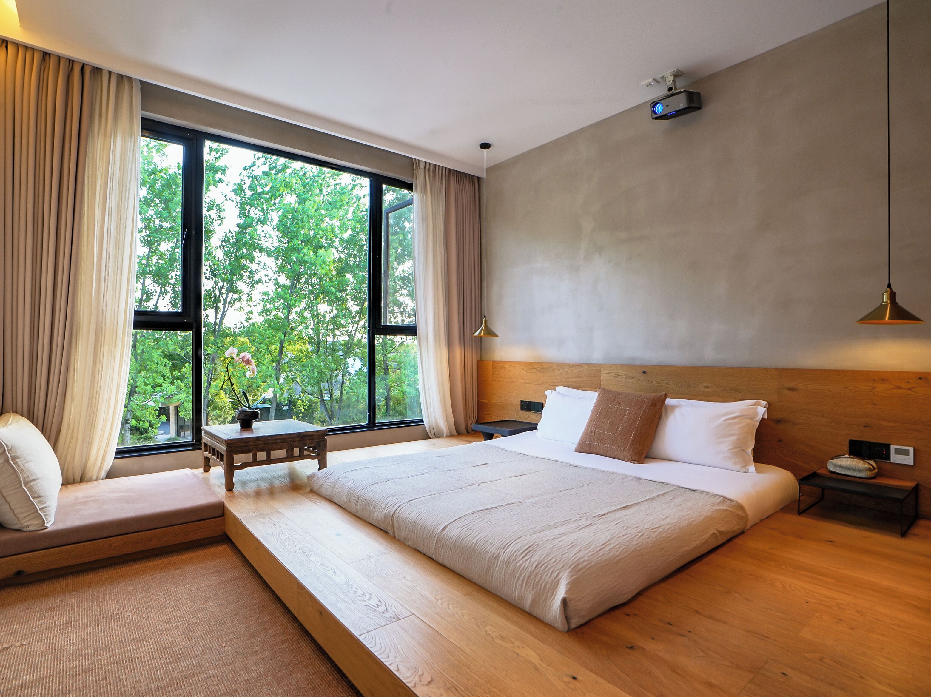 Quarto moderno com cama grande, cabeceira de madeira, mesa de cabeceira e vista para o verde lá fora.