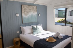 Quarto com cama, travesseiros, cobertor, chapéu e janela com vista para o exterior.