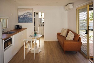 Uma cozinha compacta com mesa e cadeiras, um sofá e uma porta de vidro deslizante que dá para uma área externa.