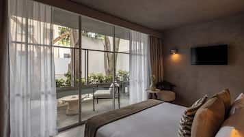 Quarto com uma janela grande, uma cama, televisão na parede e uma pequena mesa com cadeira do lado de fora.