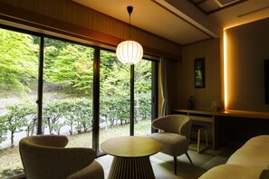 Quarto moderno com grandes janelas, uma mesa redonda, duas cadeiras, uma luminária pendente e uma pequena mesa de cabeceira.