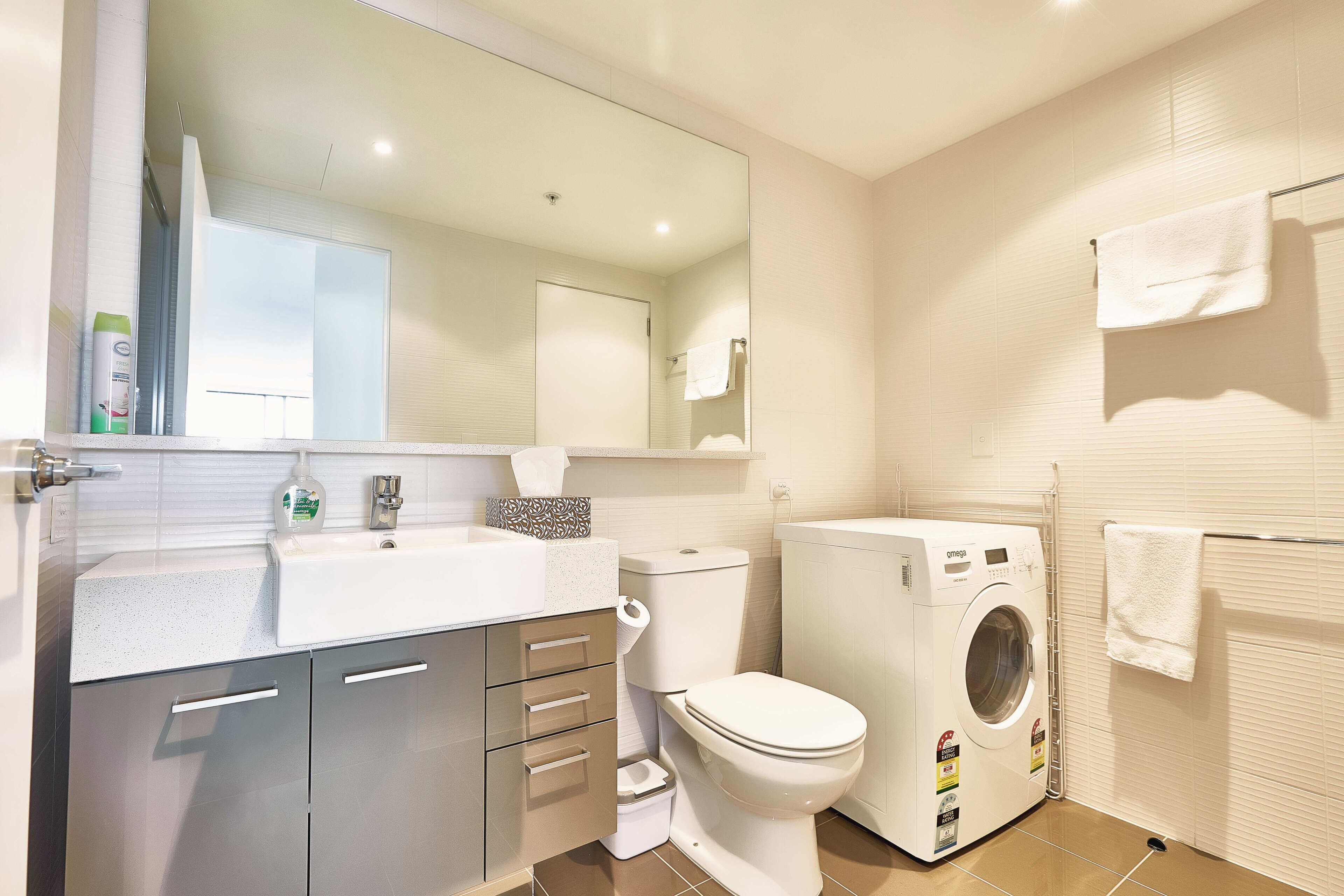 Uma casa de banho moderna com lavatório, espelho, sanita e máquina de lavar roupa.
