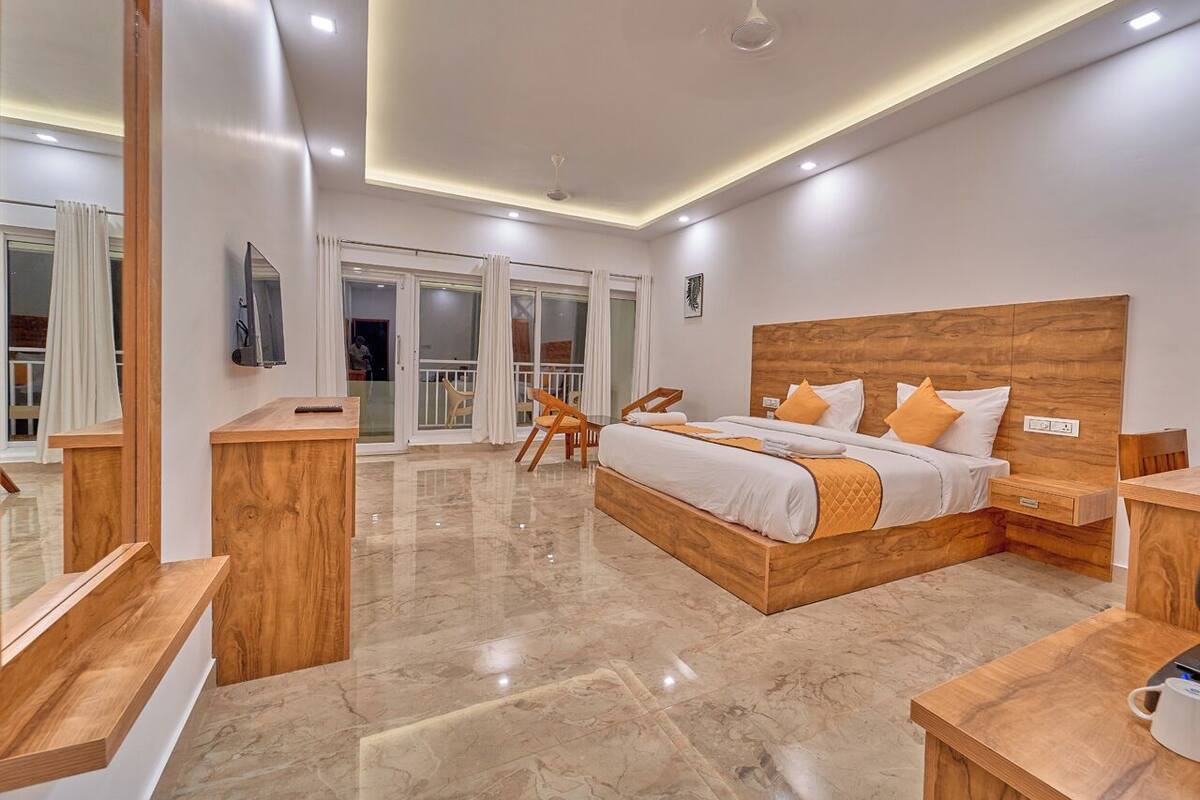 Quarto de hotel moderno com uma cama grande, móveis de madeira, um espelho e vista para o exterior.