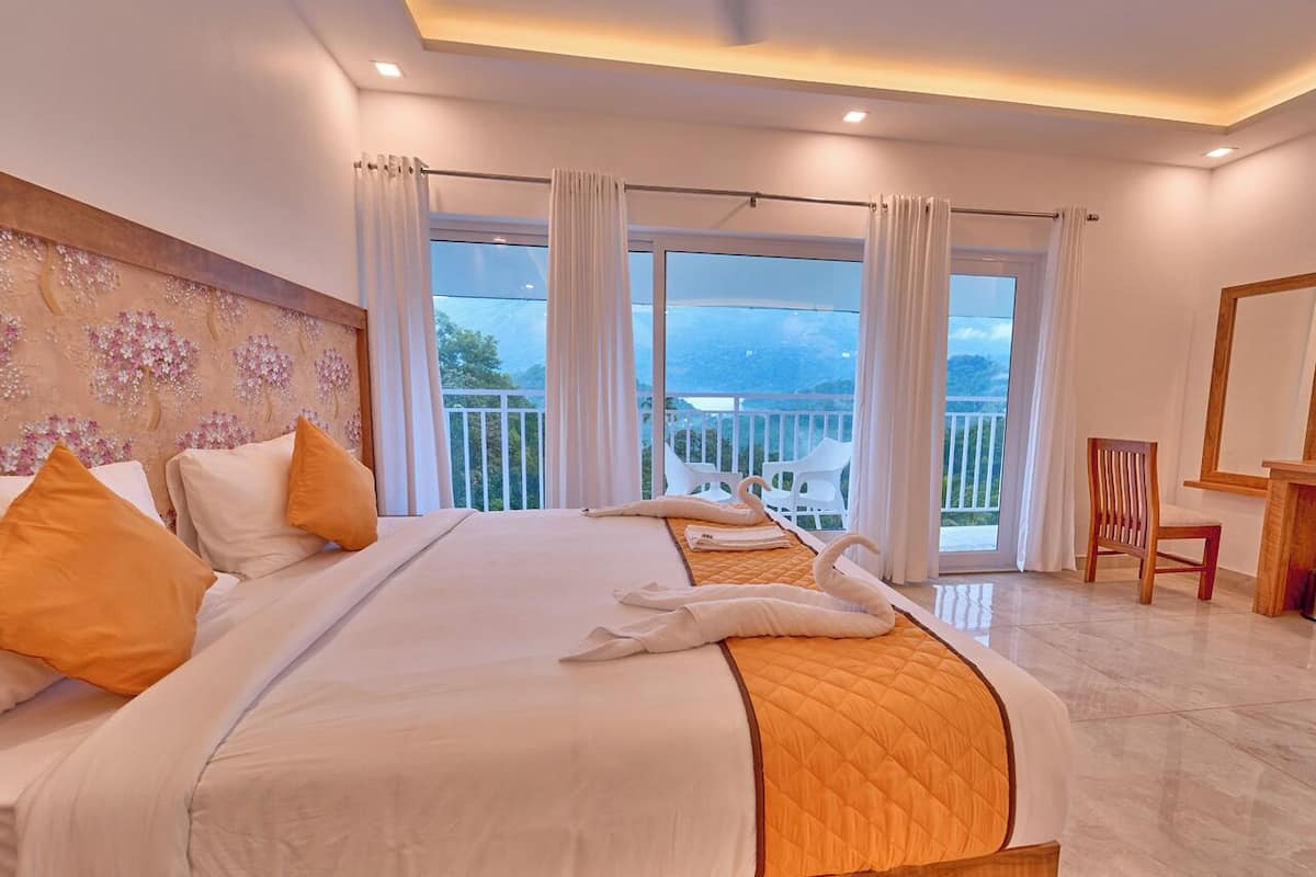 Quarto de hotel com uma cama grande, uma varanda com cortinas e vista para as montanhas.