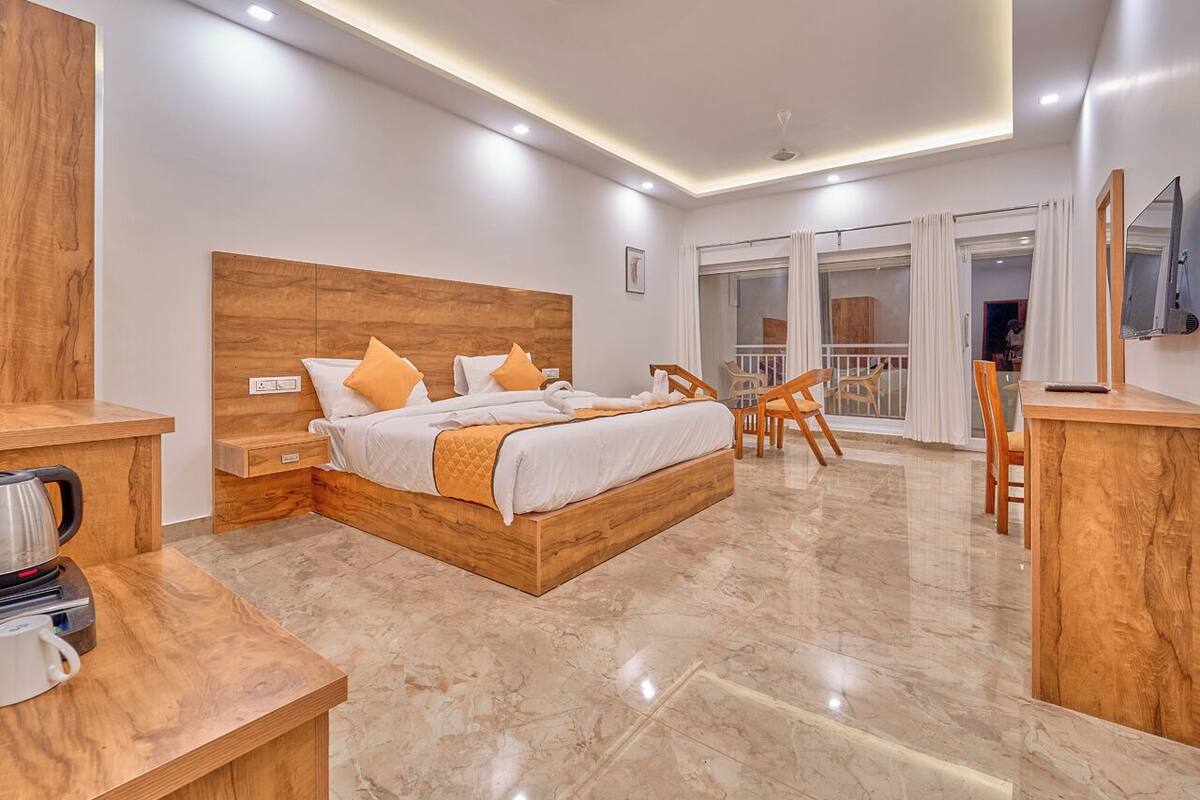 Quarto de hotel moderno com cama de madeira, escrivaninha, cadeira e varanda com cortinas.