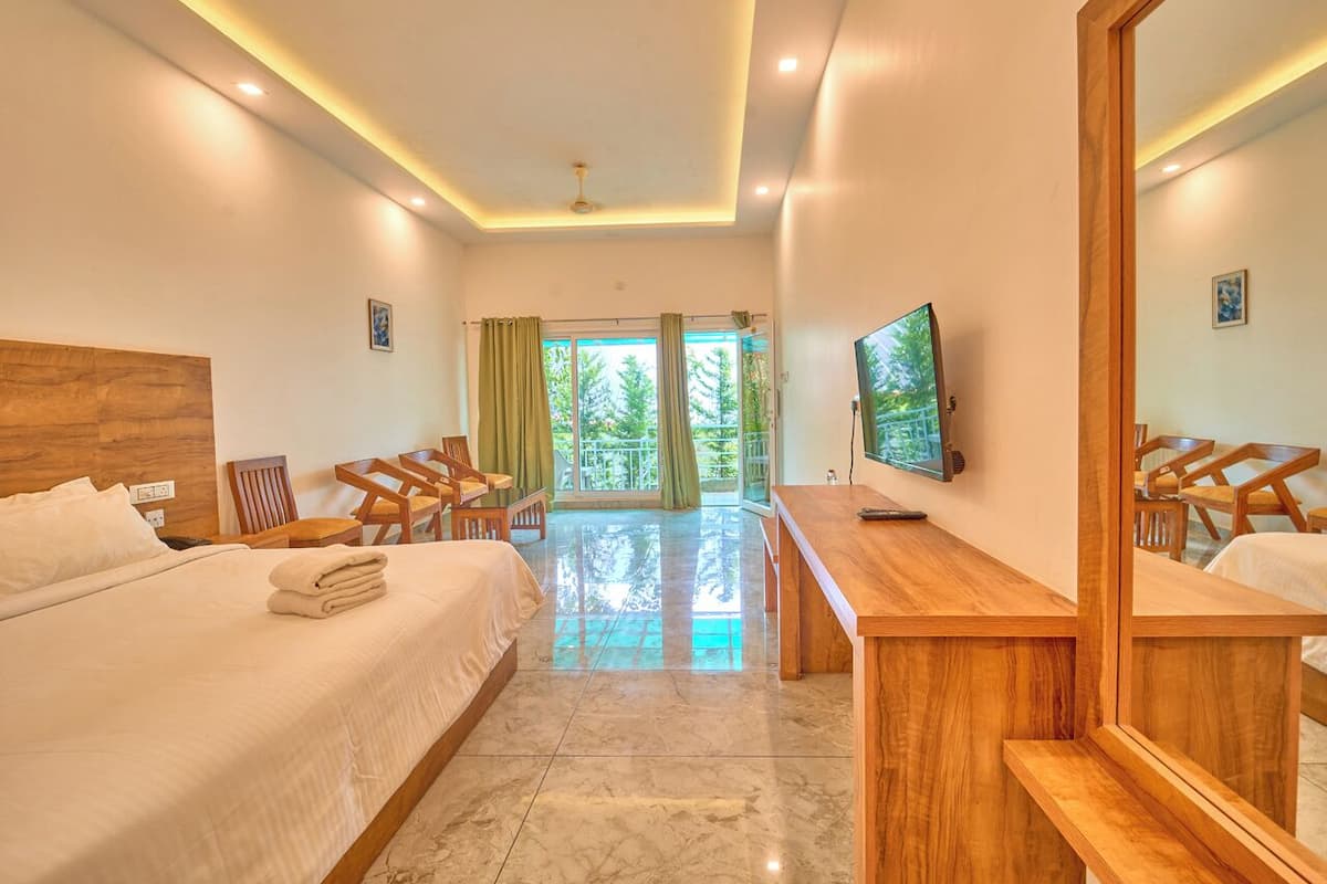 Quarto de hotel com cama, escrivaninha, televisão e varanda com cortinas.