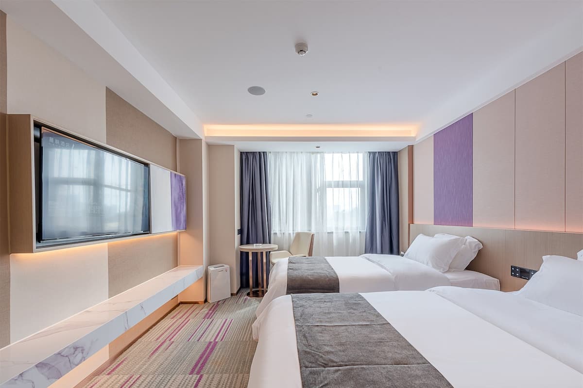 Quarto de hotel com duas camas, uma televisão, uma mesinha e uma cadeira.