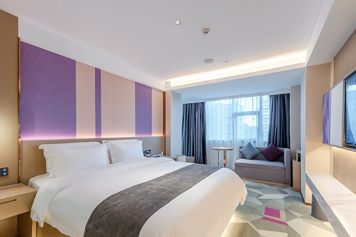 Quarto de hotel com cama, sofá, mesa pequena e televisão.