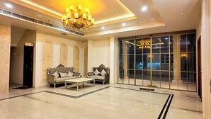 Um hall amplo com um candelabro, um conjunto de sofás e uma grande porta de vidro que dá para o exterior.