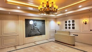 Uma área de recepção com piso de mármore, uma grande escultura na parede, um lustre e quadros emoldurados.