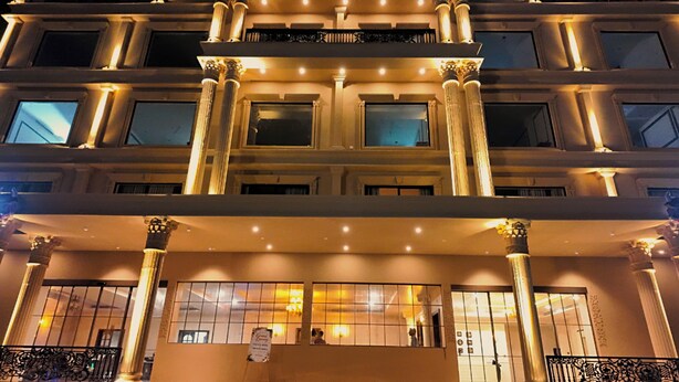 Um hotel com vários andares e arquitetura clássica, com colunas, janelas amplas e uma entrada bem iluminada.