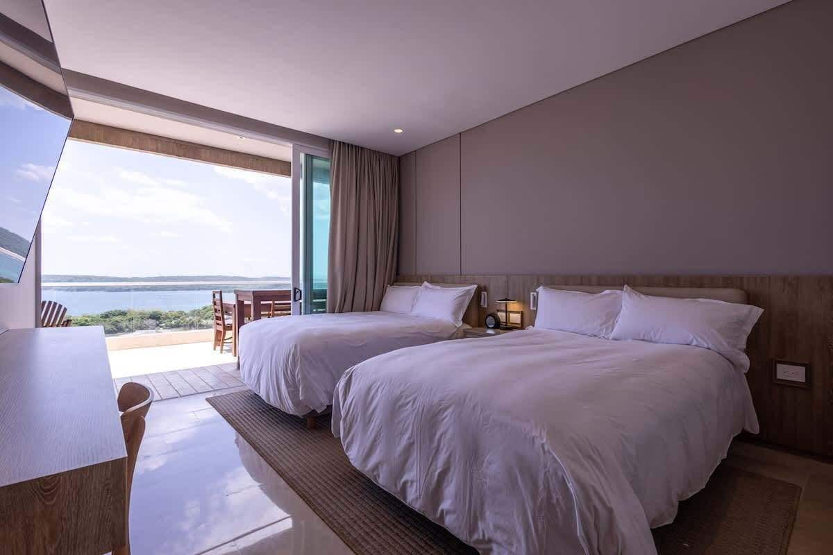 Quarto de hotel com duas camas, uma mesa de jantar e vista para o mar.