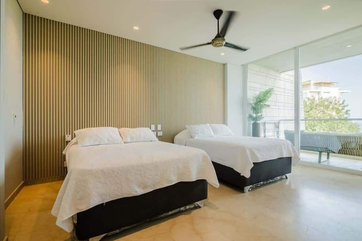Quarto de hotel moderno com duas camas, um ventilador de teto e uma varanda com vista.
