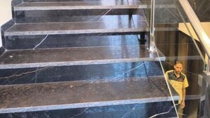 Uma escadaria de mármore com guarda-corpos de vidro que dá acesso a um elevador.