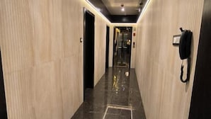 Um corredor com piso de mármore, painéis de madeira clara e um telefone na parede.