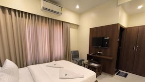 Quarto de hotel com cama, televisão, escrivaninha e guarda-roupa.