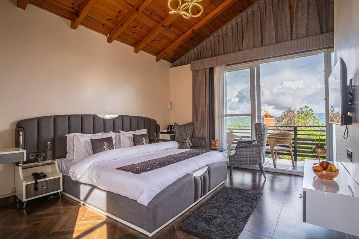 Quarto com uma cama grande, mesa de cabeceira, cadeira, televisão e vista para o exterior.