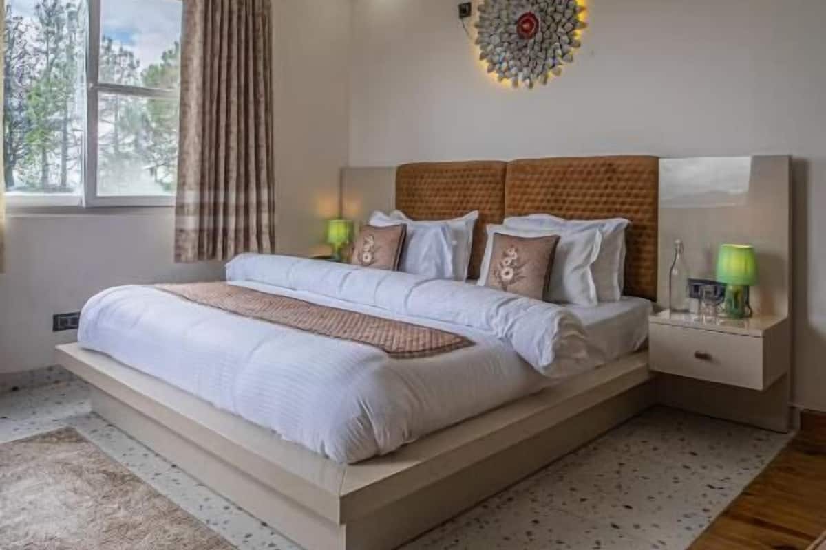 Quarto moderno com uma cama grande, cabeceira com iluminação decorativa, mesa de cabeceira com abajur e janela com cortinas.