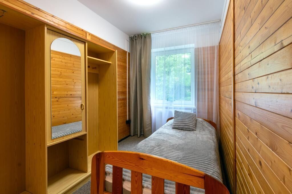 Um quarto com um guarda-roupa de madeira, uma cama com colcha cinzenta e uma janela com cortinas.