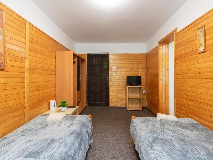 Quarto com duas camas, paredes de madeira, televisão e porta.