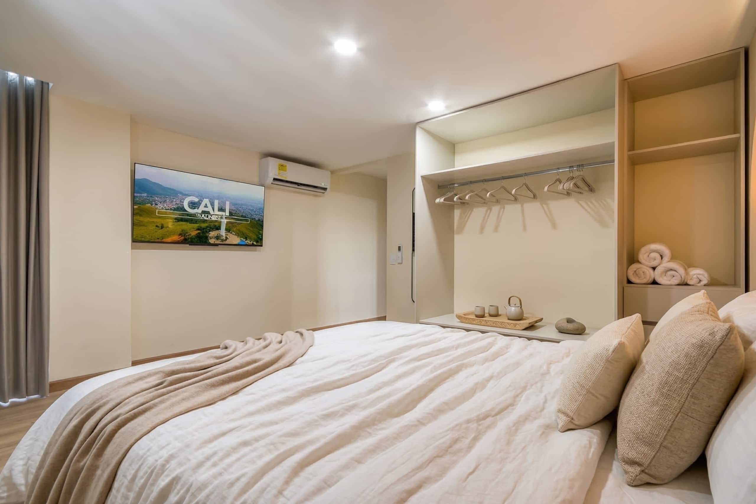 Quarto de hotel com cama, guarda-roupa, espelho, porta-toalhas e televisão na parede exibindo uma vista panorâmica.