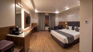 Quarto de hotel com cama, escrivaninha, cadeira e televisão.