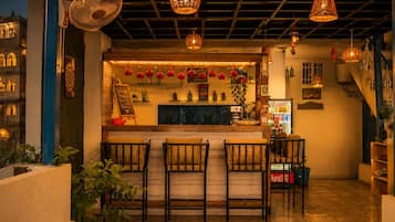 Uma área de bar com balcão, assentos e detalhes decorativos como luminárias pendentes e adornos nas paredes.