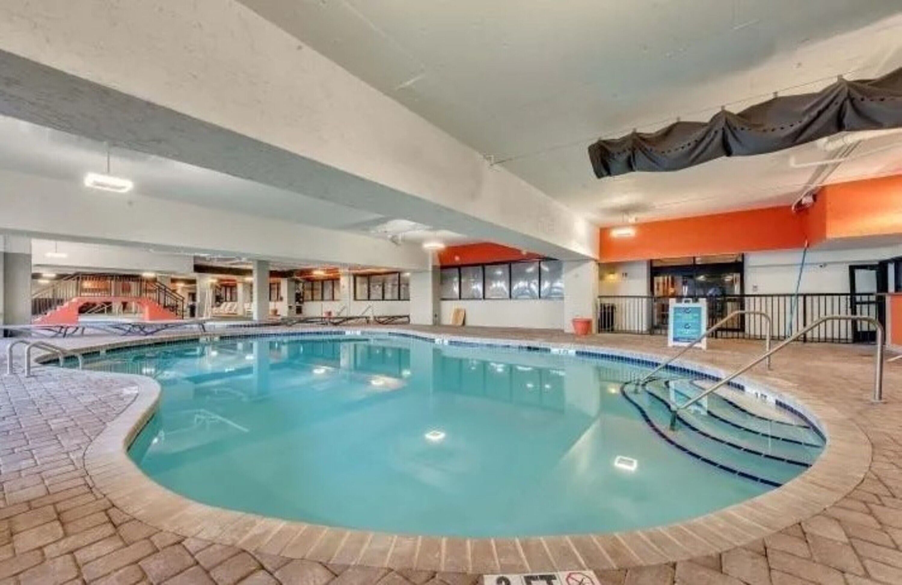 Uma piscina interior com um deck revestido de azulejos, uma escadaria que desce para um andar inferior e uma placa indicando zona proibida.