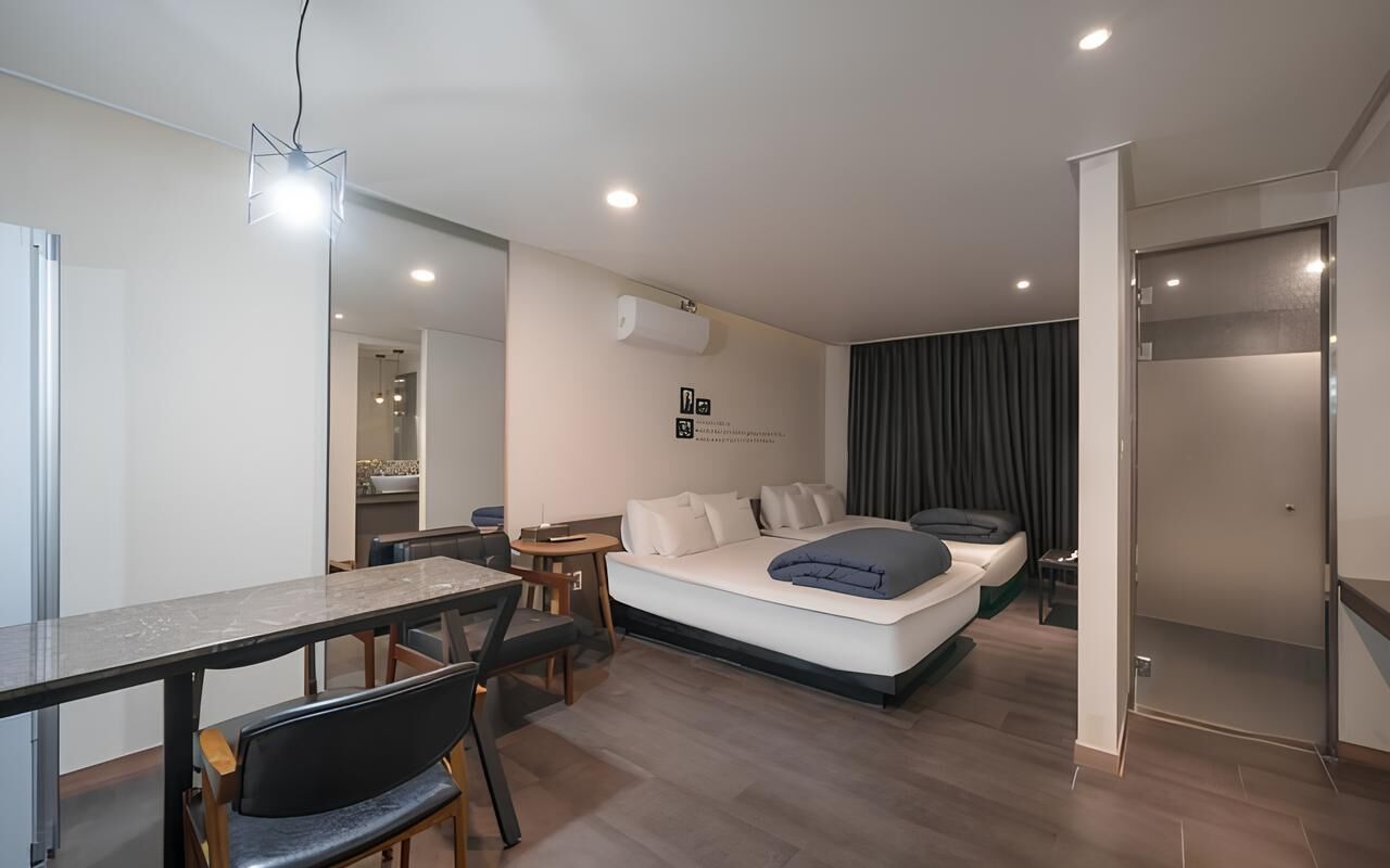 Uma sala de estar moderna com um sofá, uma mesa de jantar com cadeiras e uma cozinha ao fundo.
