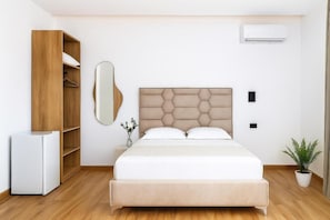 Quarto com cama, guarda-roupa, espelho, planta em vaso e ar condicionado.
