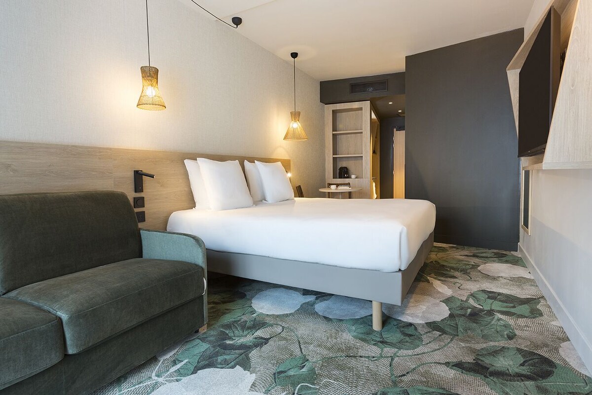 Quarto de hotel moderno com cama, sofá, uma mesinha e estante.