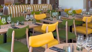 Interior de restaurante com várias mesas, cadeiras e luminárias pendentes.