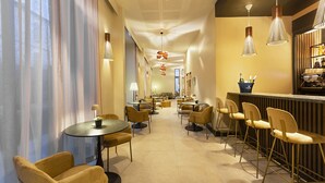 Um hall de hotel com mesas e cadeiras redondas, área de bar e teto com iluminação decorativa.