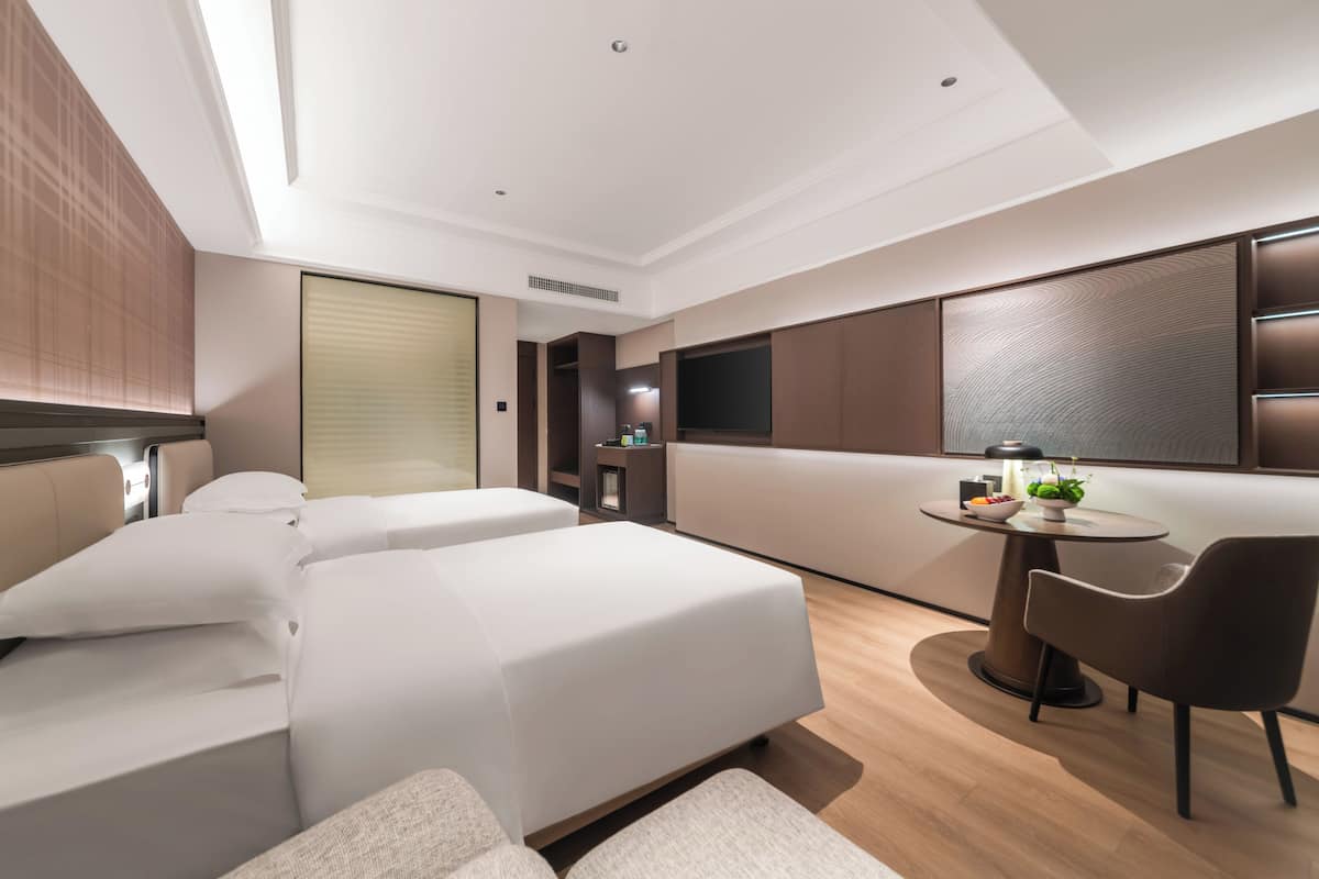Quarto de hotel moderno com uma cama grande, uma escrivaninha, uma cadeira e uma pequena mesa com uma planta.