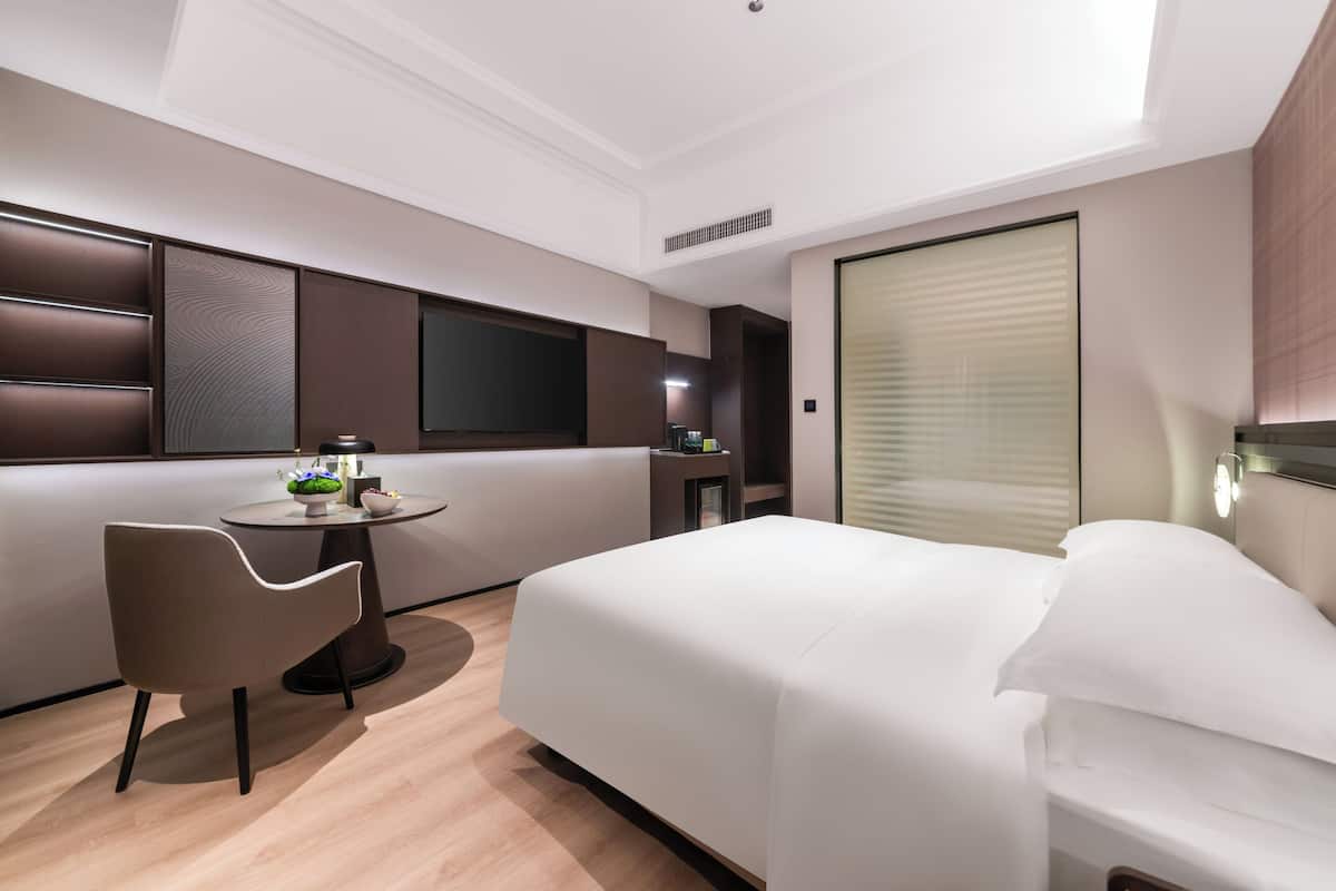 Quarto de hotel moderno com uma cama, uma escrivaninha, uma cadeira e uma janela com persianas.