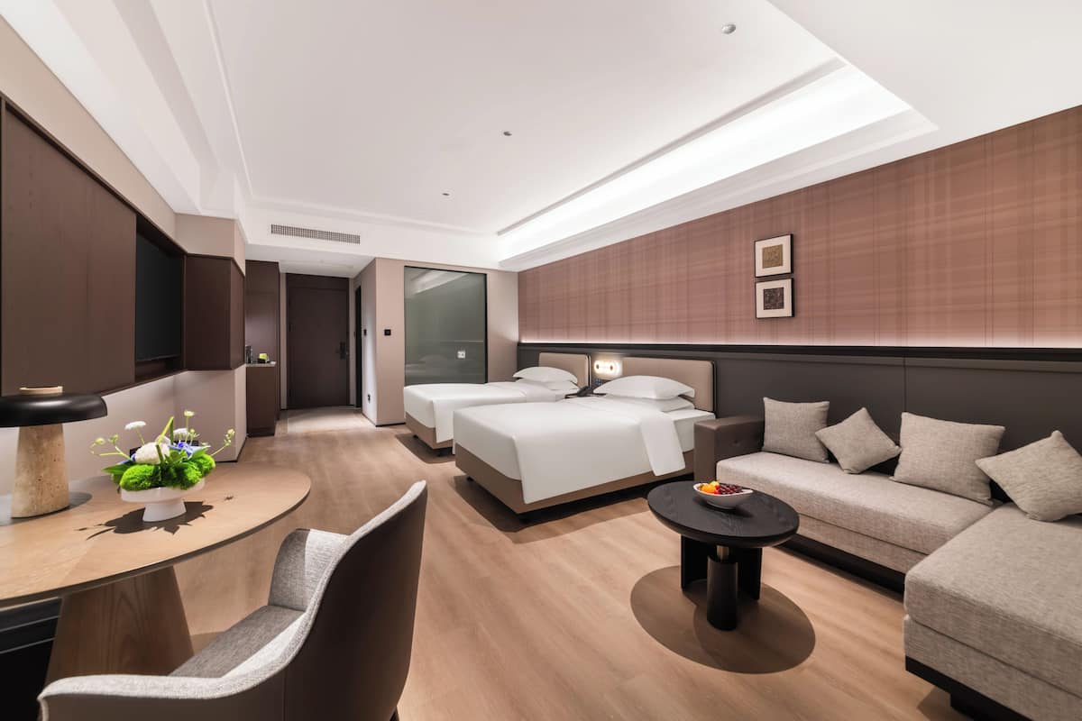 Quarto de hotel moderno com cama, sofá, escrivaninha e uma pequena mesa com um vaso de flores.