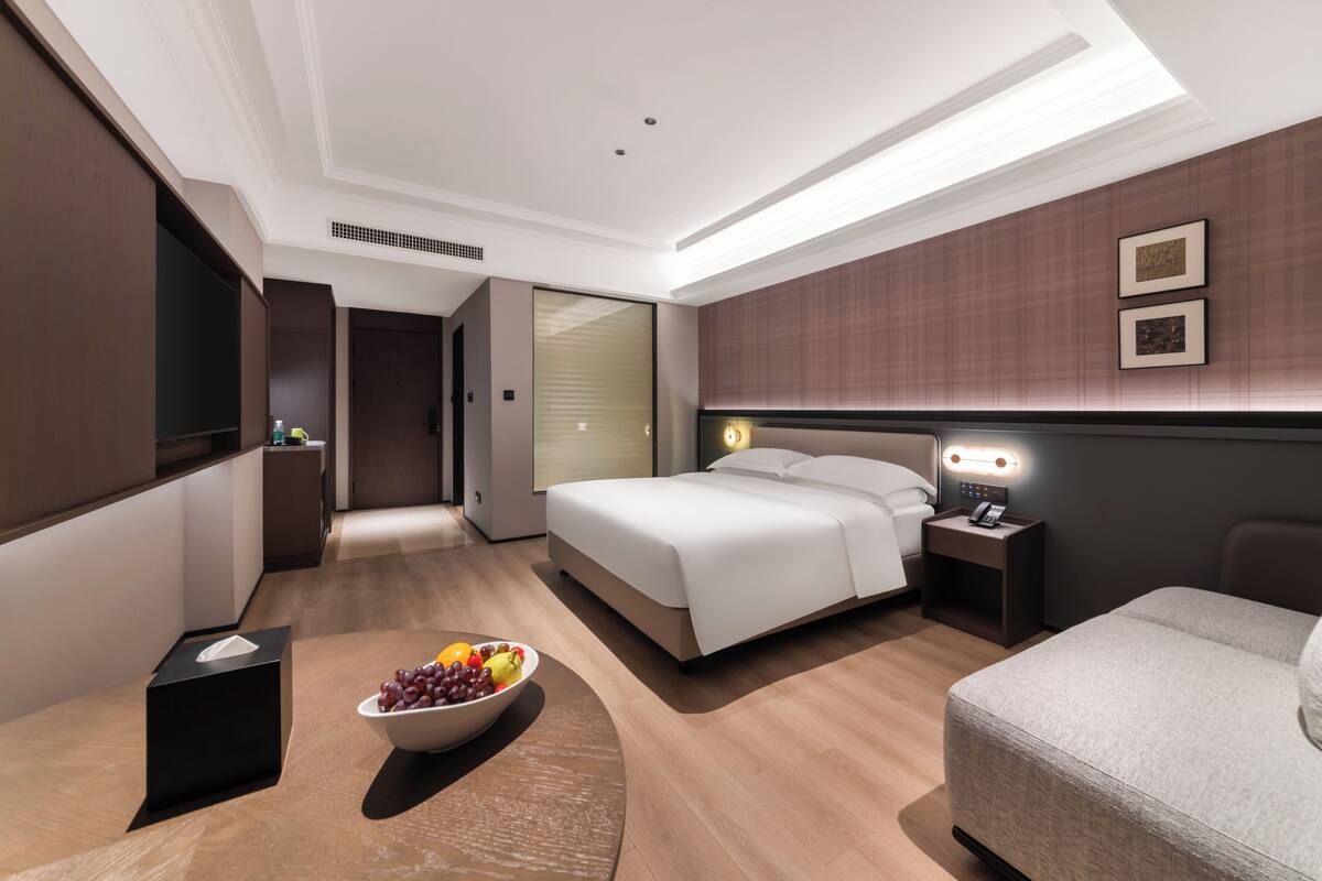 Quarto de hotel moderno com uma cama grande, mesa de cabeceira e uma cesta de frutas.