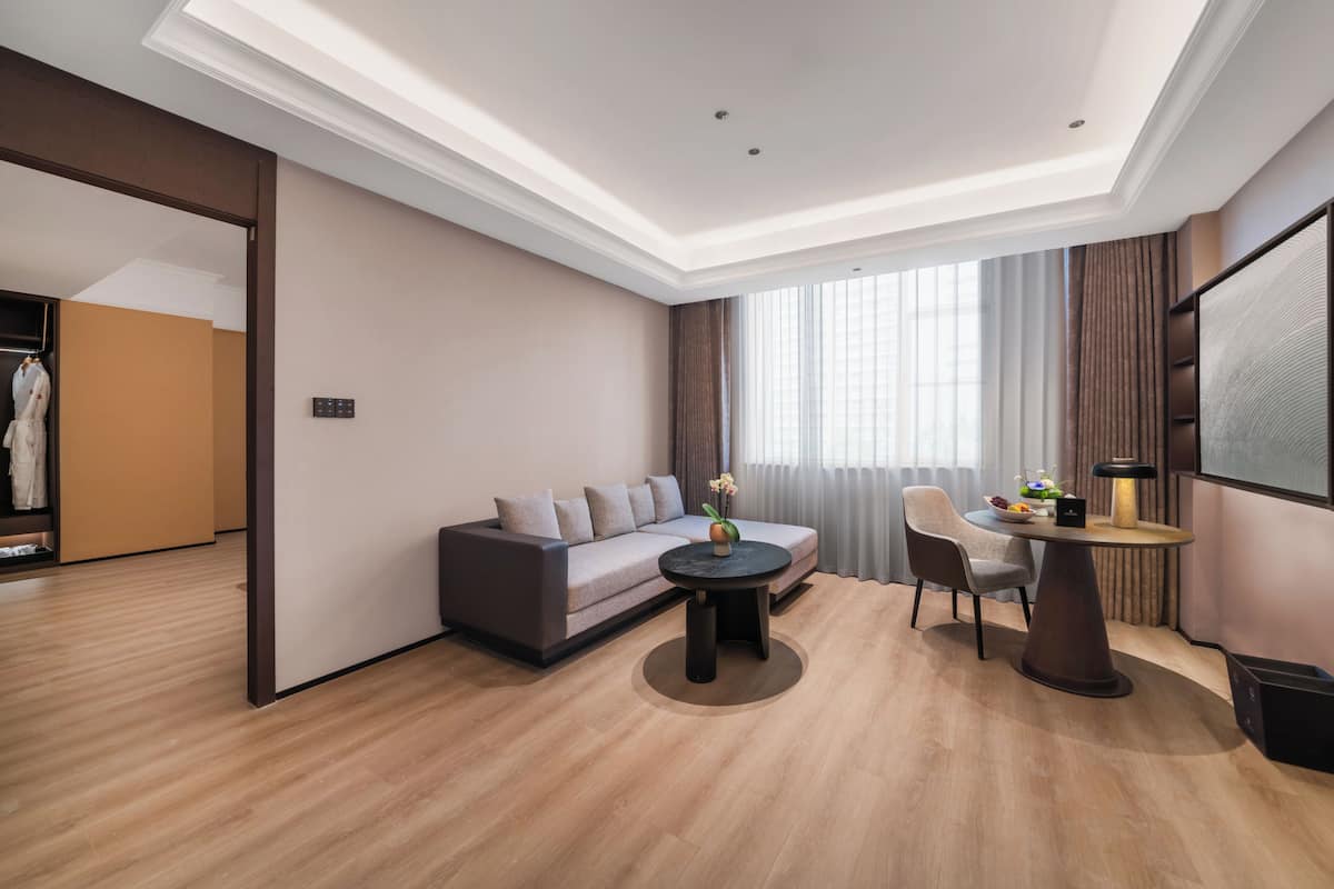 Quarto de hotel moderno com sofá, mesa de centro redonda, mesa de jantar e televisão.