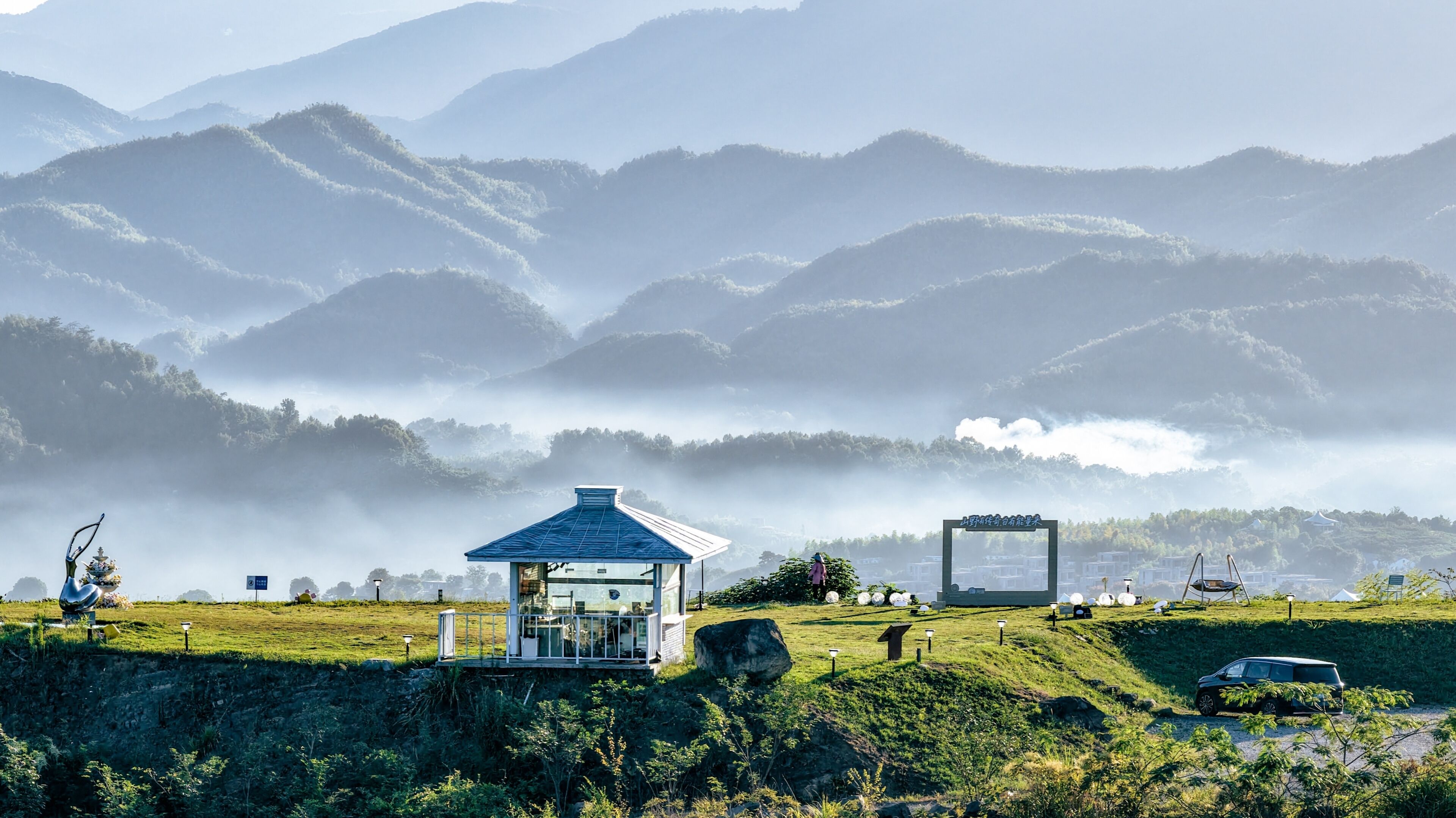 Estrutura de estufa com telhado azul, cercada por uma paisagem gramada com colinas suaves e névoa ao fundo.