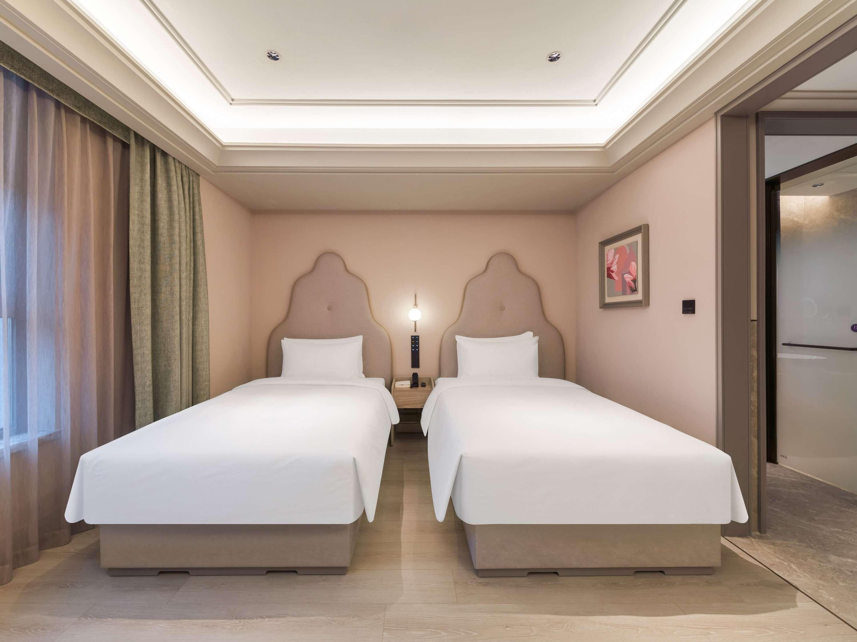 Quarto de hotel com duas camas, uma mesinha de cabeceira, um abajur e um quadro na parede.