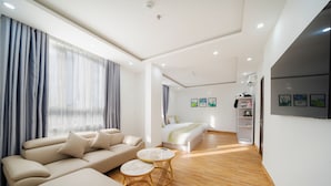 Quarto de hotel moderno com sofá, duas mesas redondas, cama e televisão.