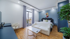 Quarto de hotel moderno com cama, sofá, escrivaninha, cadeira, planta em vaso e vista da cidade.