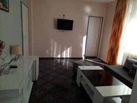 Quarto com televisão de tela plana na parede, sofá branco, mesa de centro e mesa de jantar.