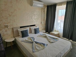 Quarto de hotel com cama, uma mesinha redonda, uma cadeira, ar condicionado e vista para o exterior.