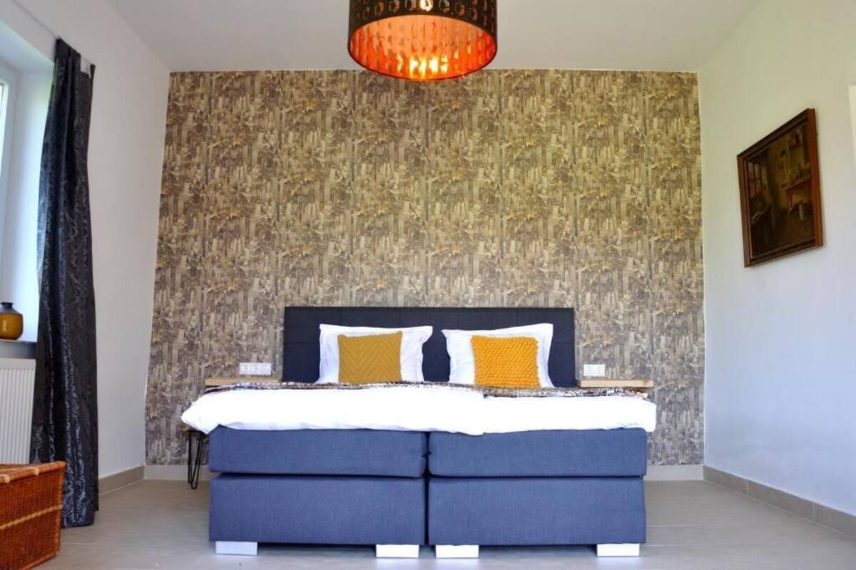 Quarto com cama grande, parede texturizada, luminária pendente e pintura na parede.